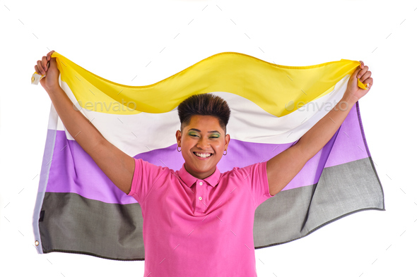non binary asian person smiling in pink shirt holding non-binary gender flag on white background ...
